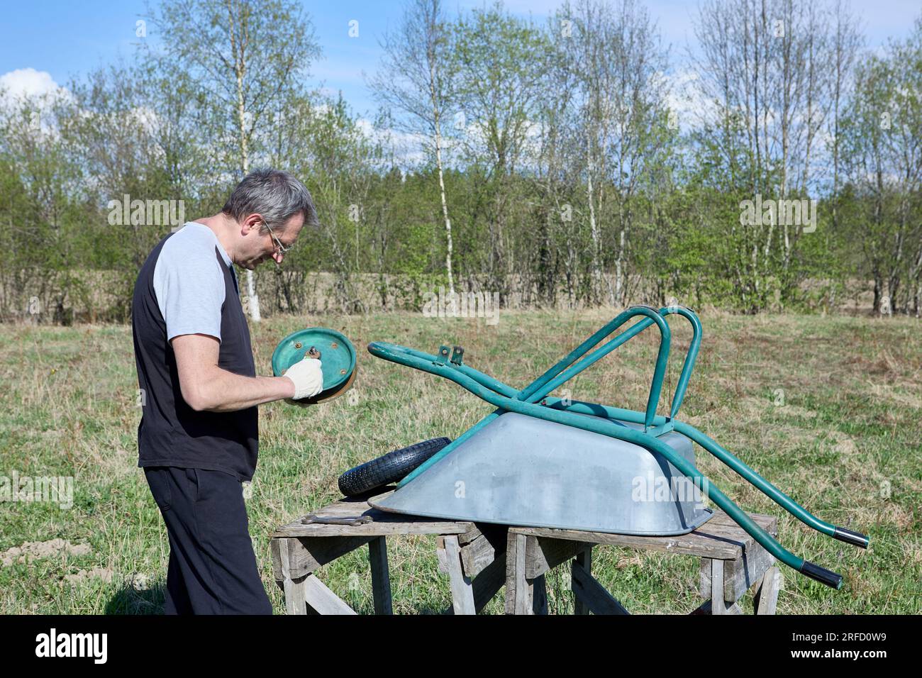 Farmer repairs garden wheelbarrow wheel outside Stock Photo - Alamy