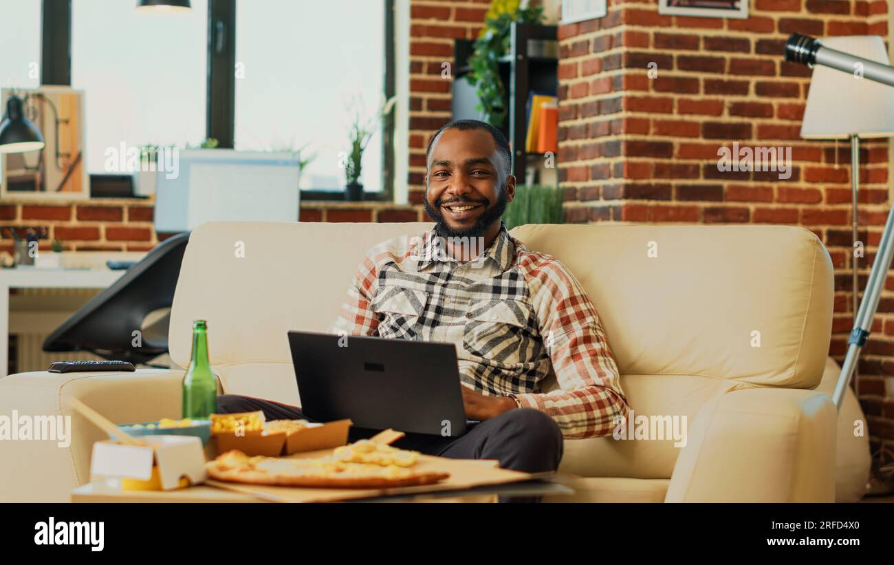 Smiling man using laptop in living room and watching tv, feeling ...