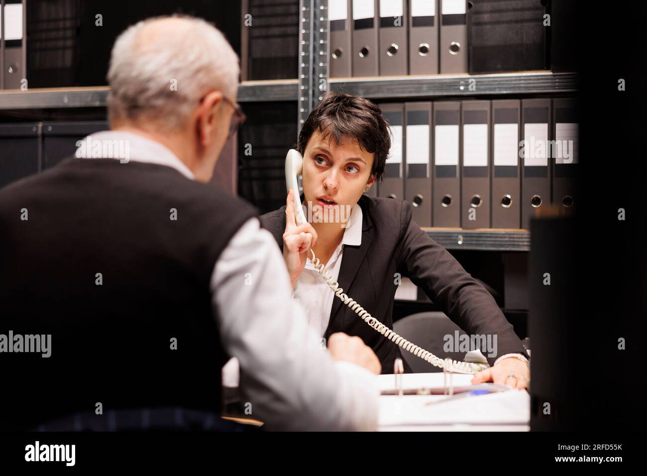 Woman investigator talking at landline phone with remote inspector ...