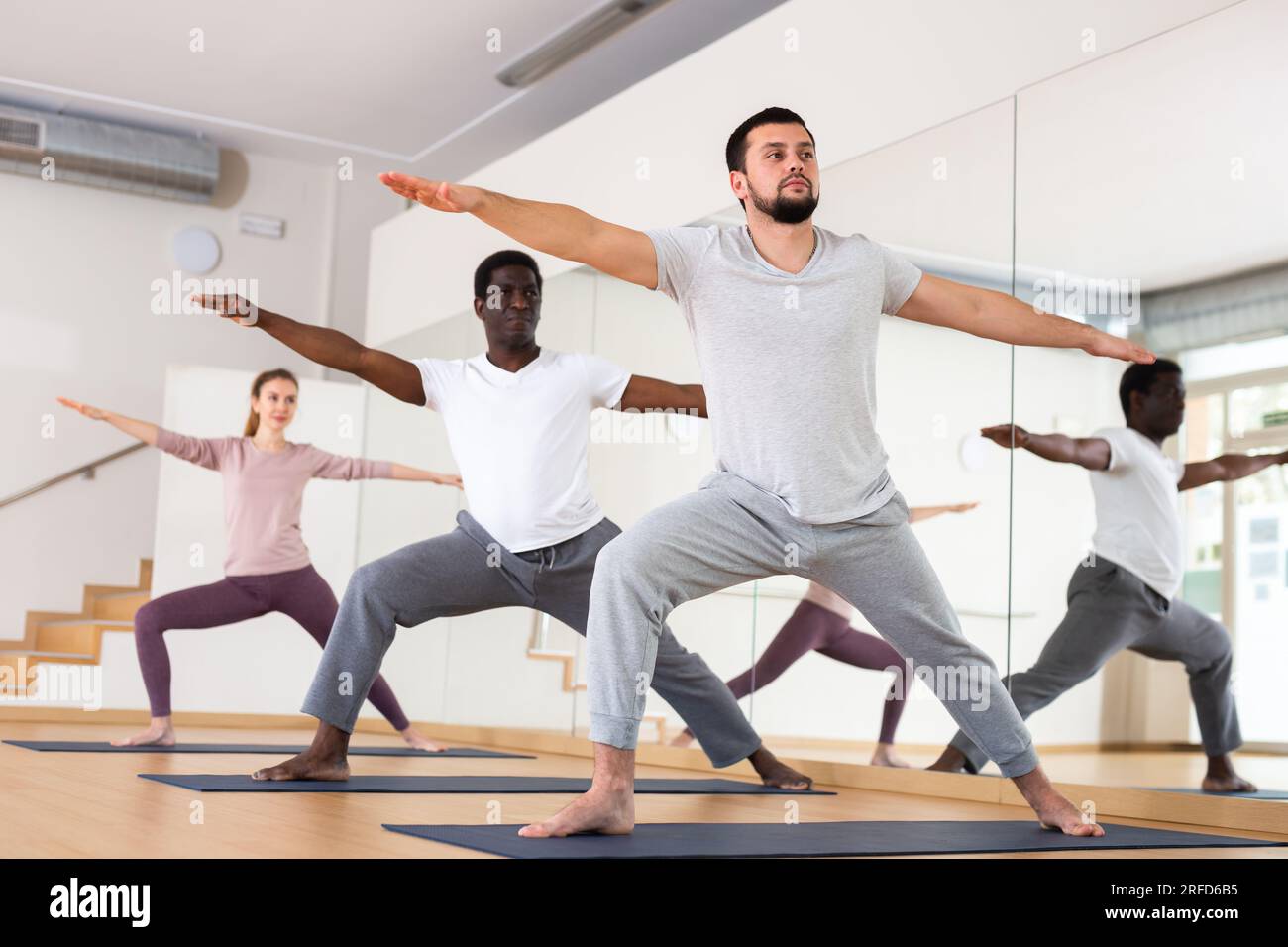 Man practising warrior two pose with group in gym Stock Photo - Alamy
