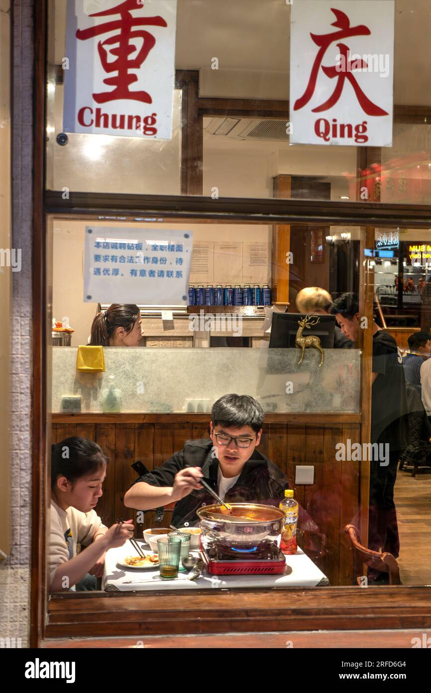 Chinese restaurant window 'CHUNG QING' with Chinese children diners enjoying a traditional ...