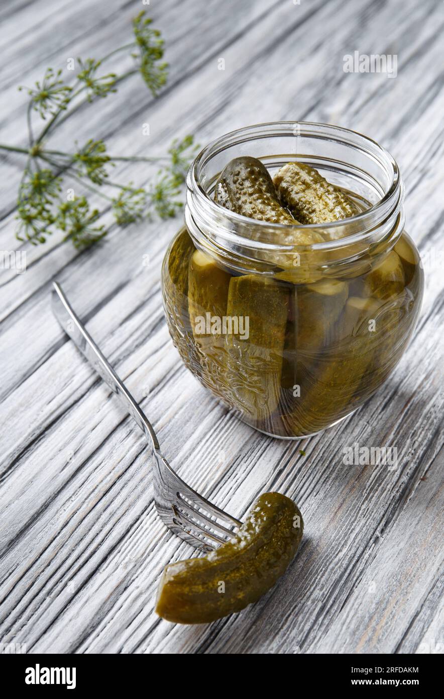 Homemade canned cucumbers in an open jar, one gherkin on a fork lies ...