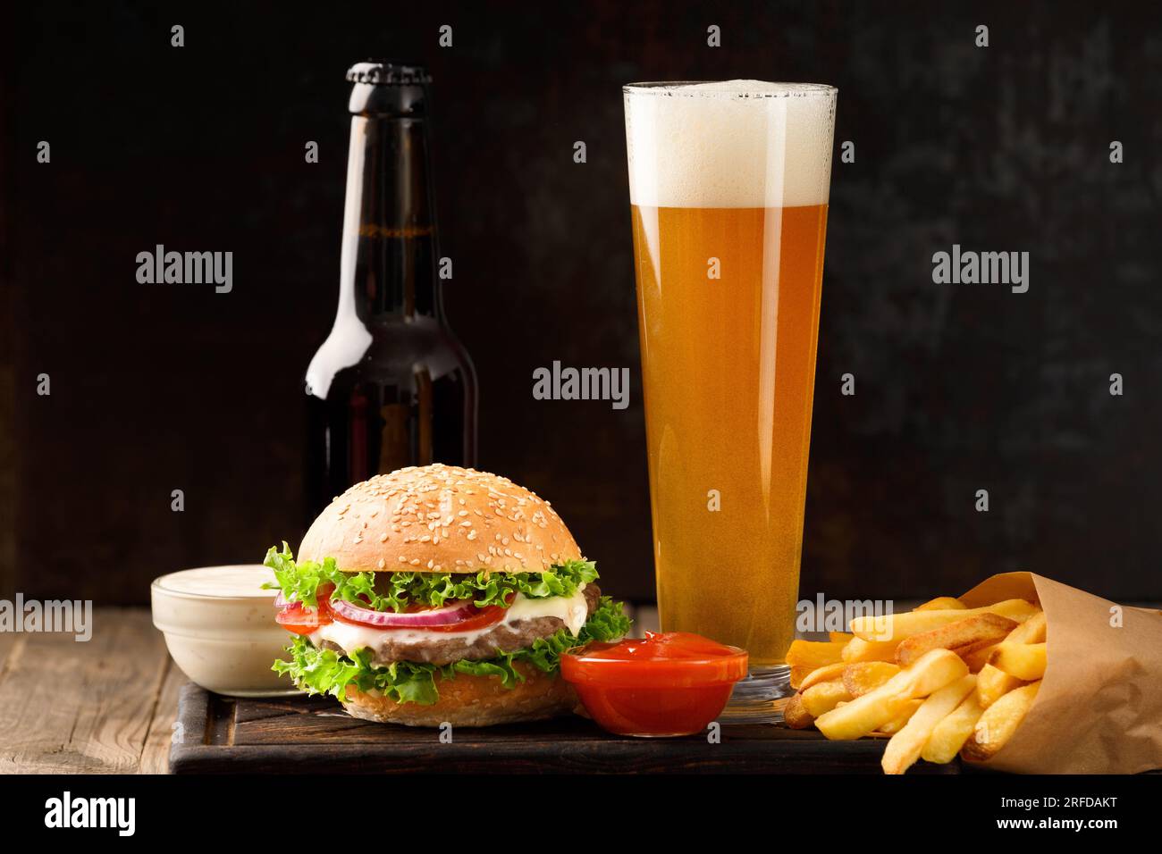Burger, beer in a bottle and in a glass mug, french fries, sauce on a ...
