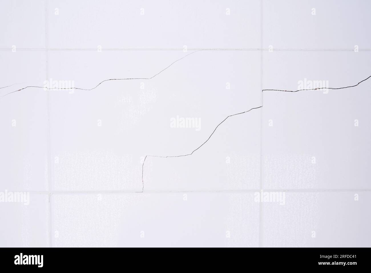 A white tiled wall with water droplets in the bathroom. Broken, cracked ...