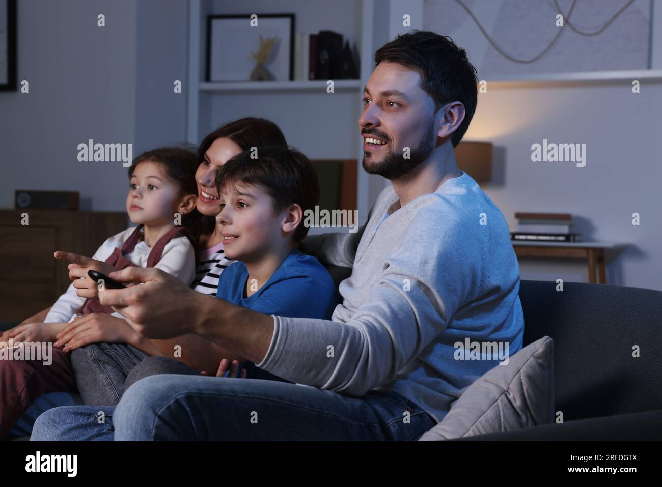 Happy family watching TV at home in evening. Father changing channels ...