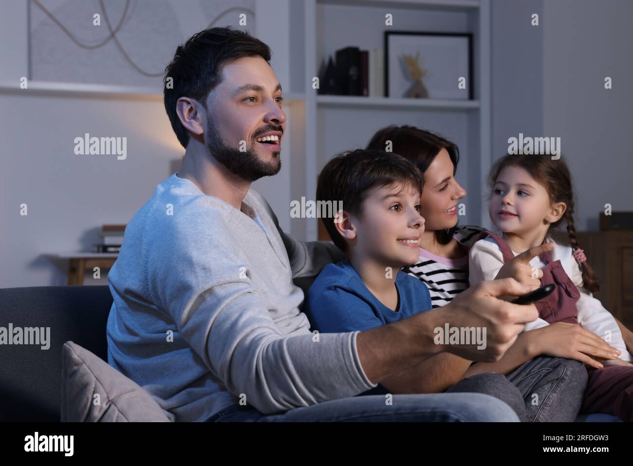 Happy family watching TV at home in evening. Father changing channels ...