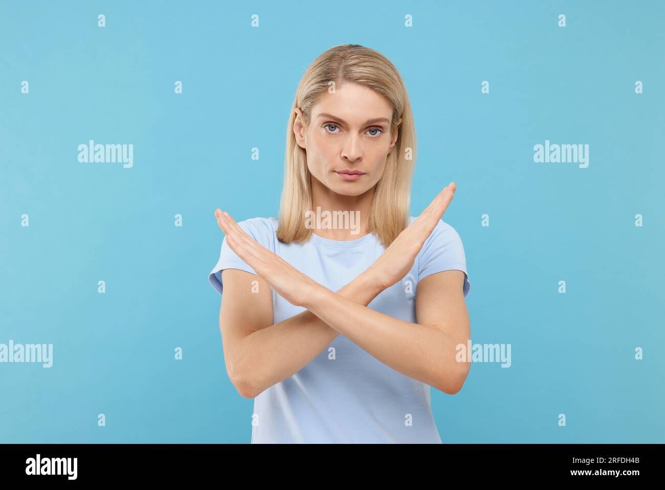 Stop gesture. Woman with crossed hands on light blue background Stock ...