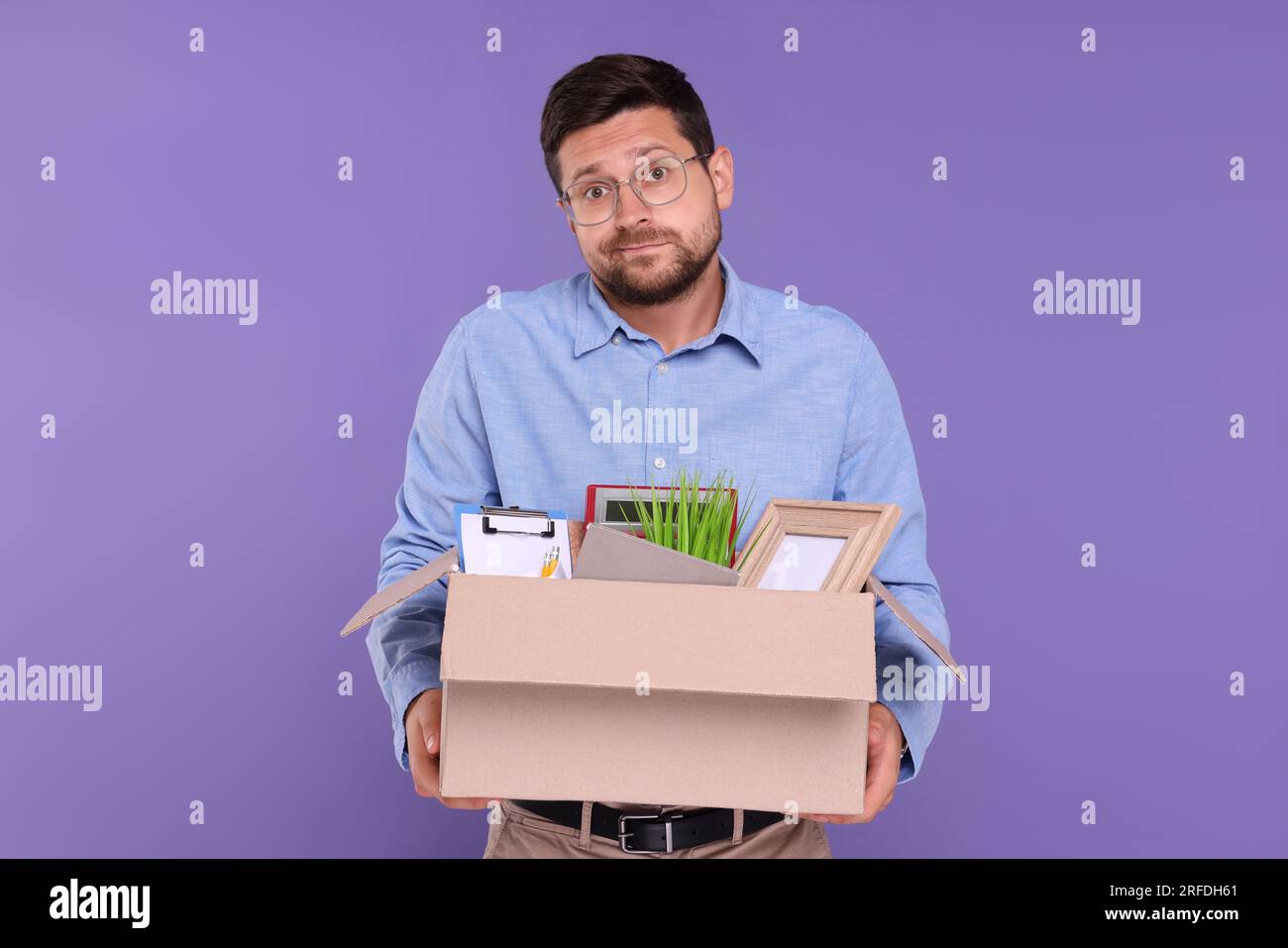 Unemployed man with box of personal office belongings on purple ...