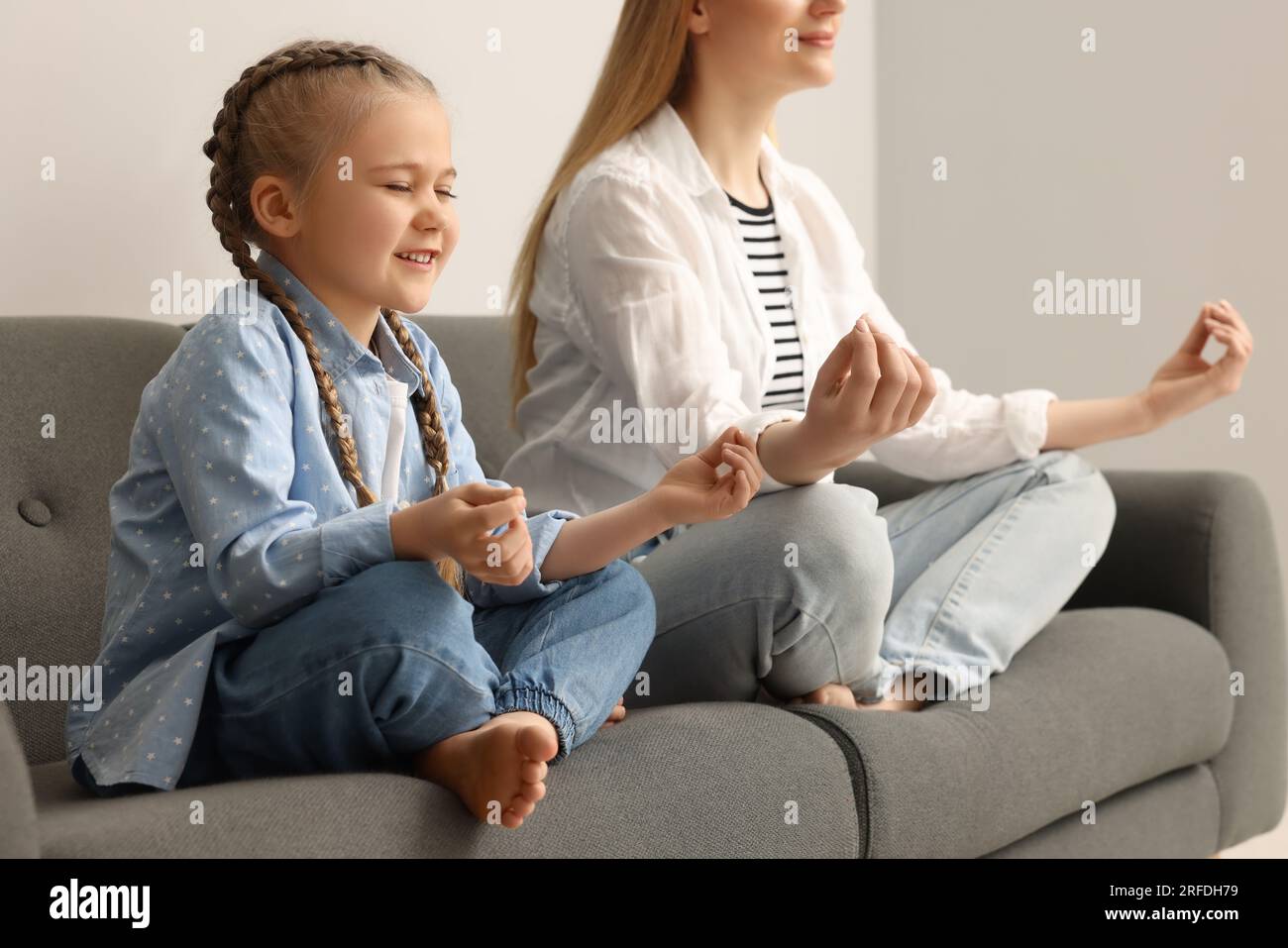 Mother with daughter meditating together on sofa indoors. Harmony and ...