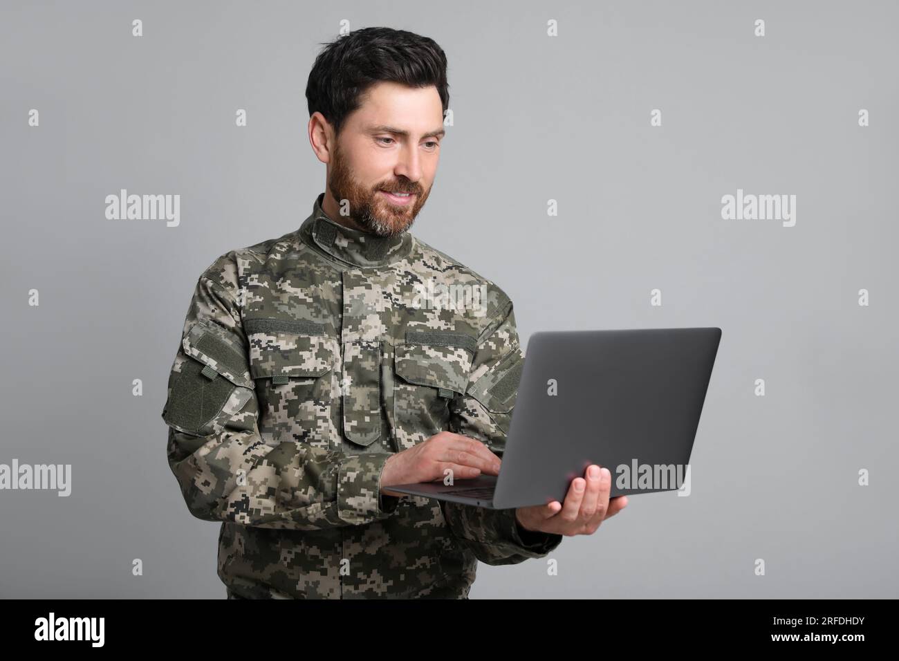 Soldier using laptop against light grey background. Military service ...