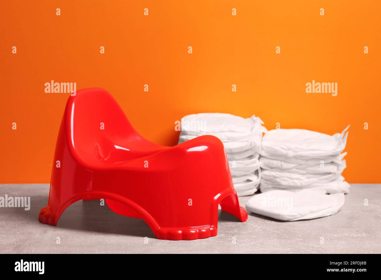 Red baby potty and diapers on stone table against orange background ...