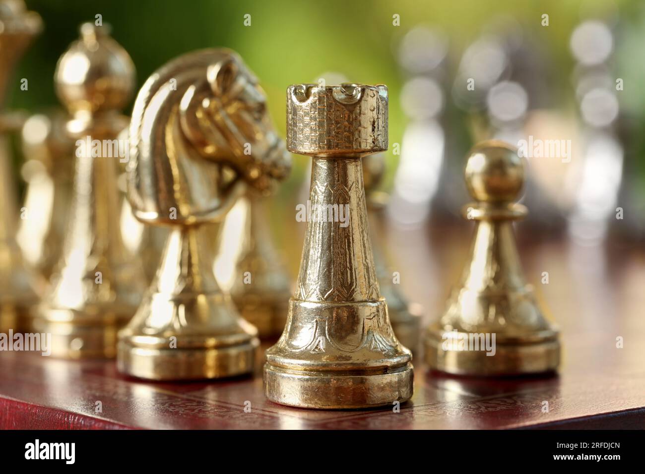 Golden rook and other chess pieces on game board against blurred ...