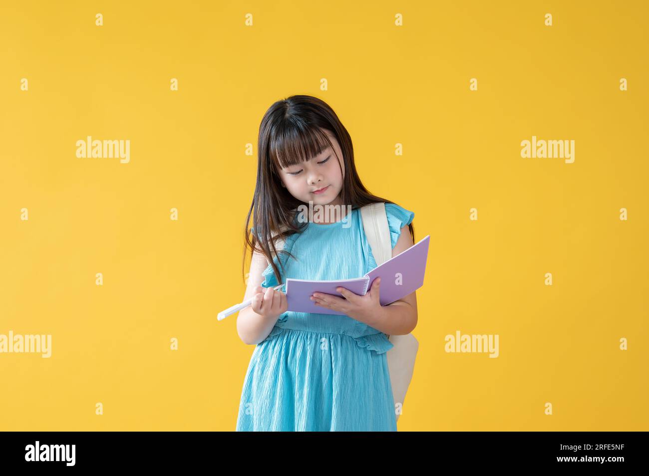 An adorable little Asian girl is writing something in her book or doing ...