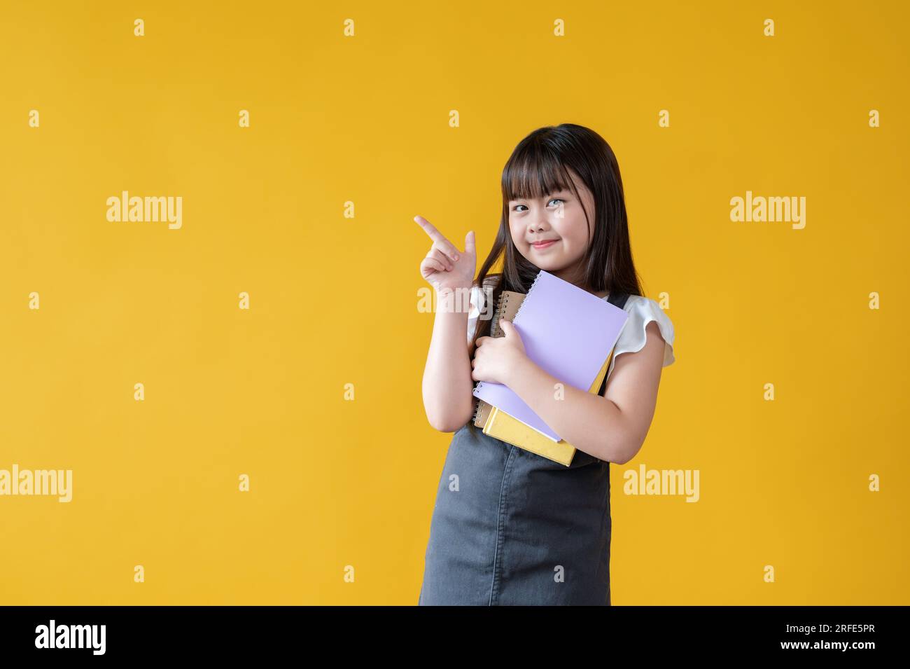 A cute little Asian girl in a cute jeans dress is pointing her finger ...