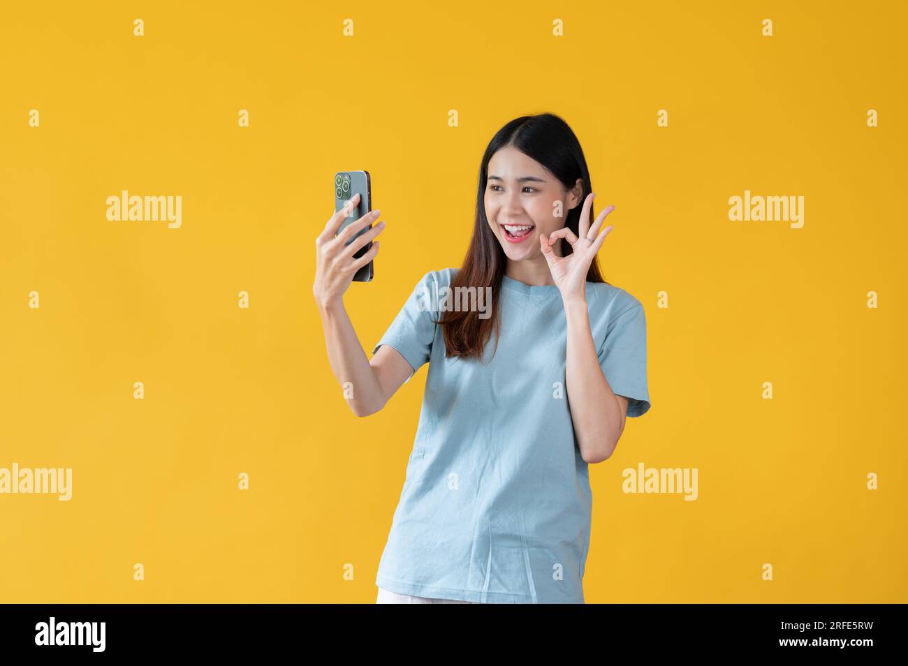 An attractive and smiling Asian woman in a blue t-shirt is showing the Okay hand sign while ...
