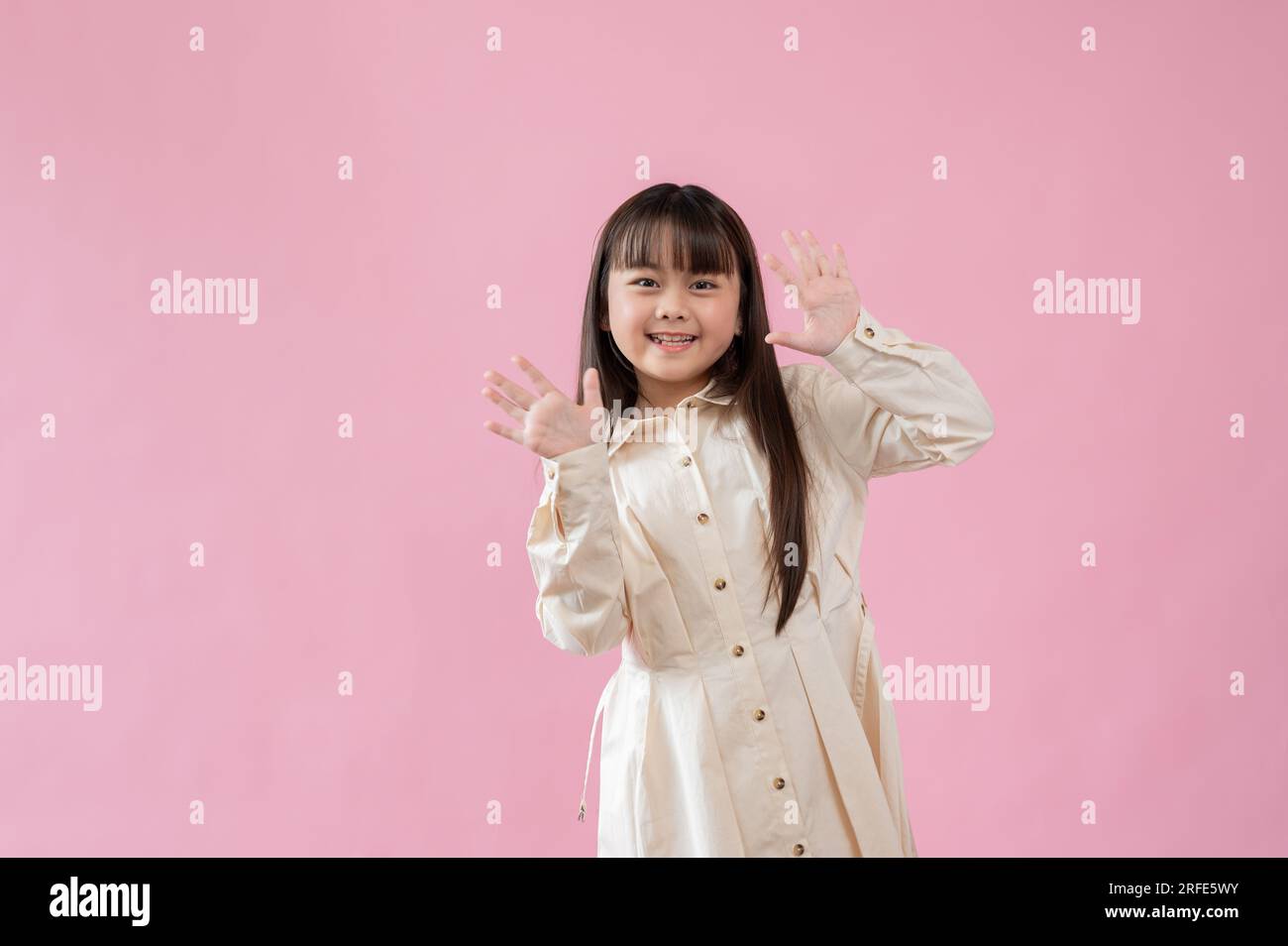 A cheerful and cute little Asian girl in a cute dress standing against ...