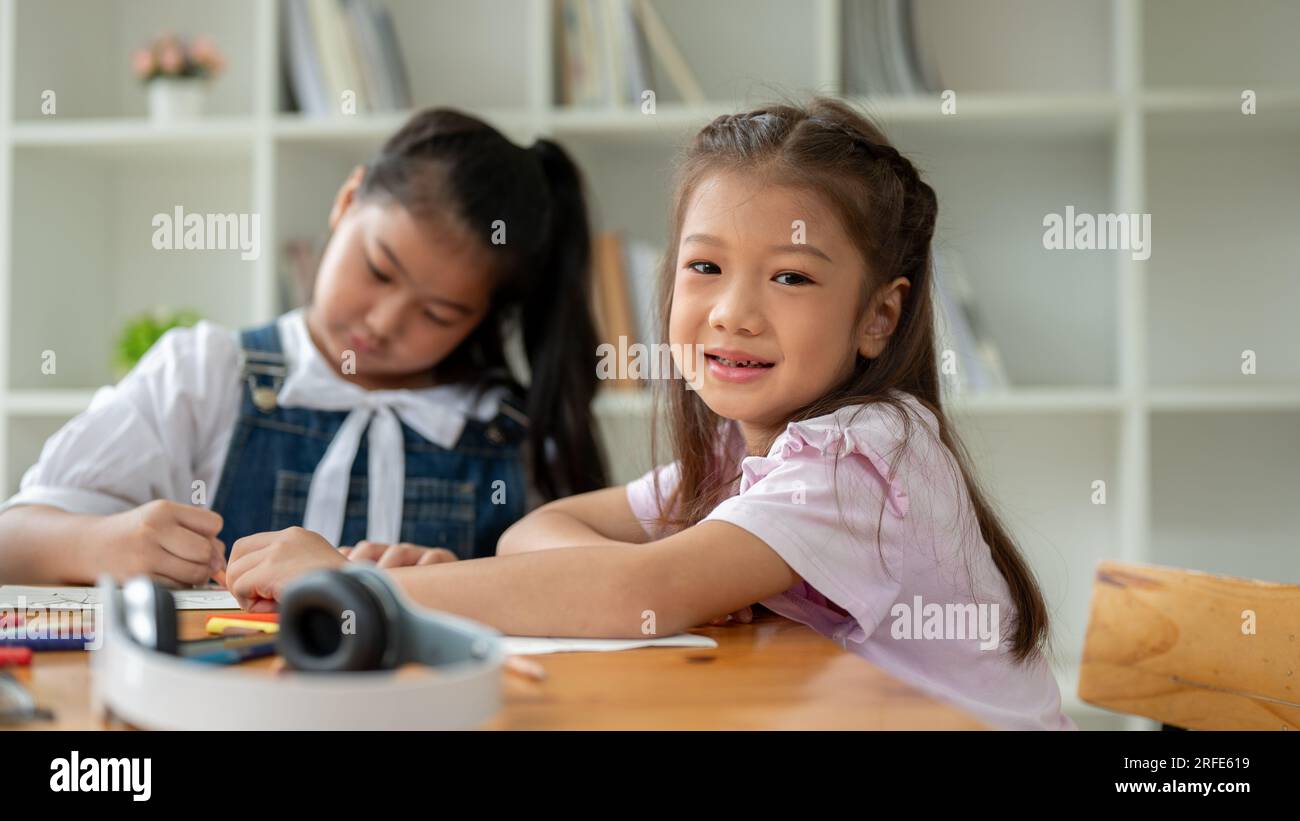 An adorable young Asian girl is sitting in the classroom, smiling and ...