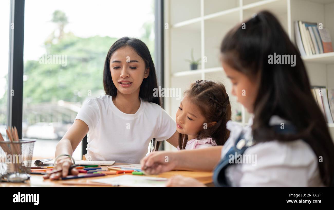A beautiful Asian female teacher or babysitter is teaching art to young ...