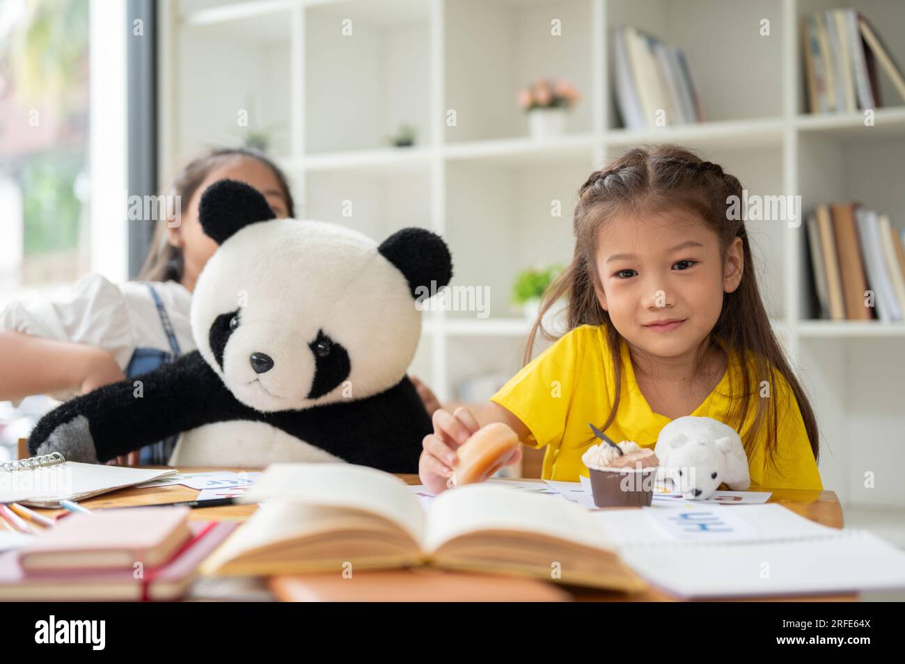 An adorable young Asian girl is sitting in the class with her friend ...