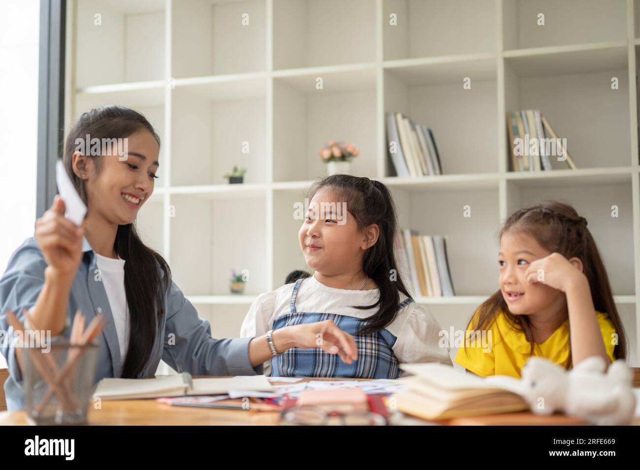 An adorable young Asian girl is enjoying studying English with a private teacher with her friend ...