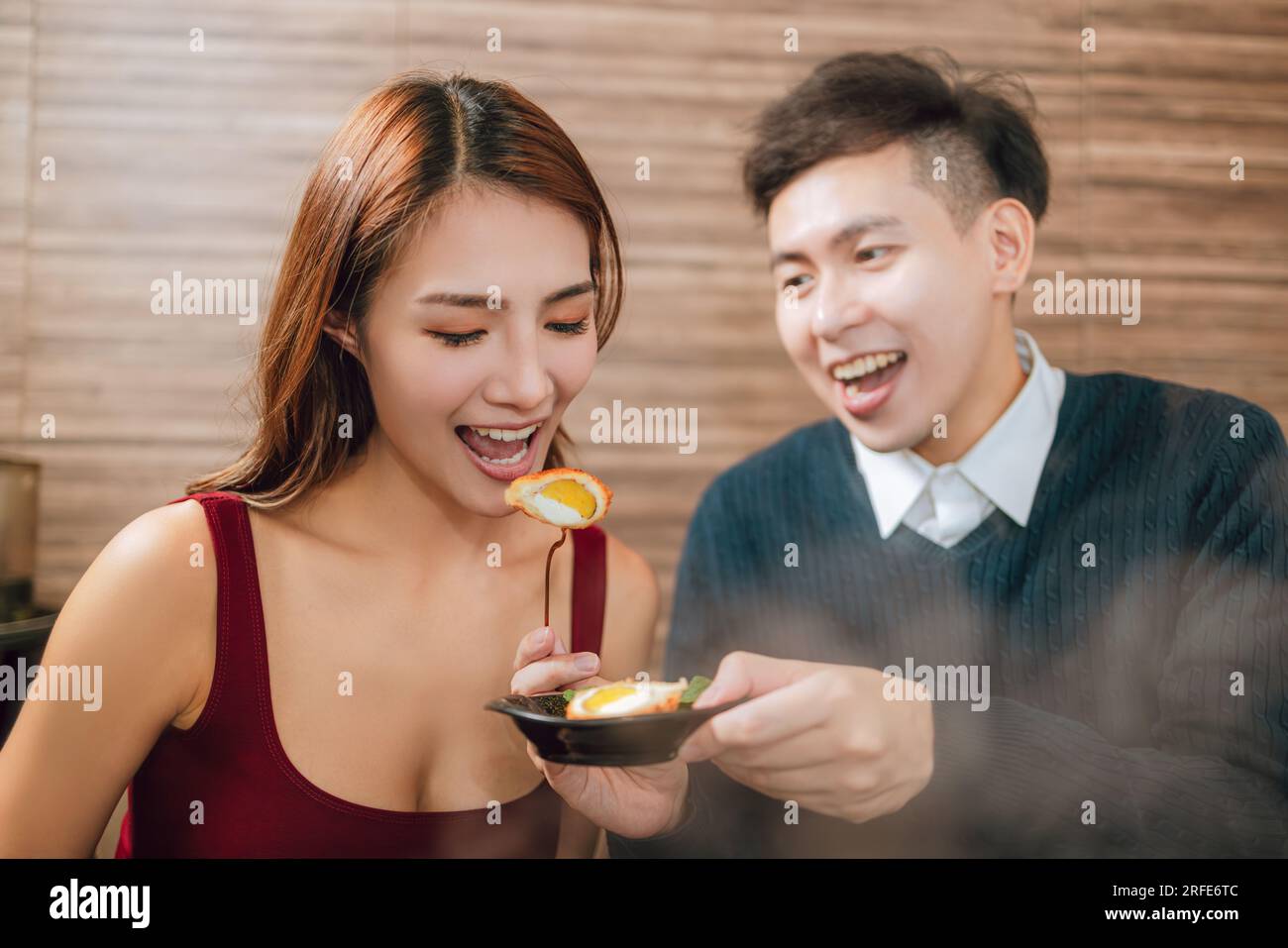 Young Asian Man Feeding Happy Girlfriend With Tasty Food In Restaurant