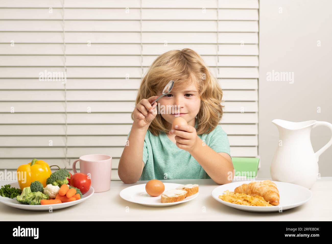 Child eating egg. Child in the kitchen at the table eating vegetable ...