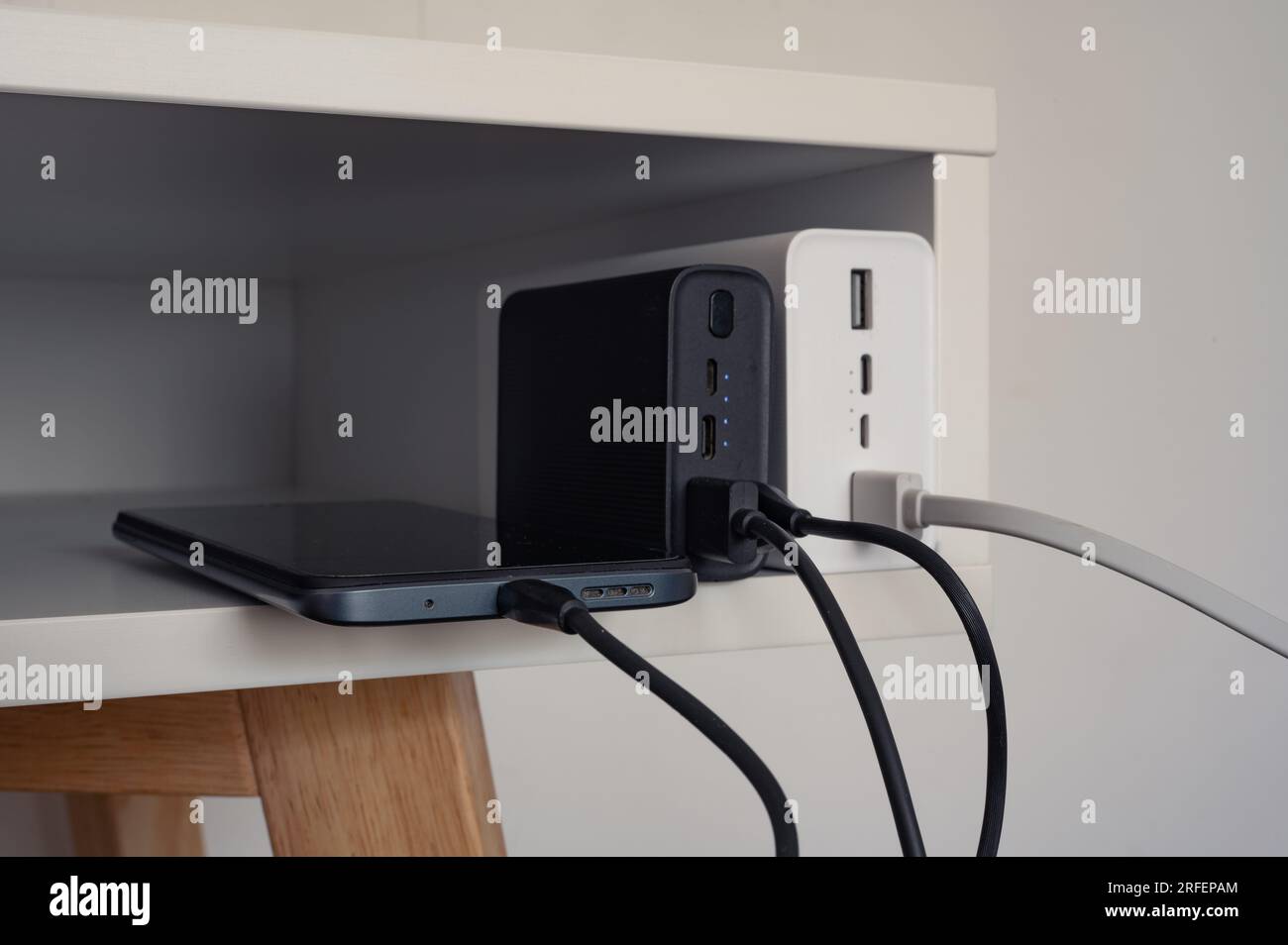 Blue smartphone charging with black power bank. Near it stands white power bank. All in white ...