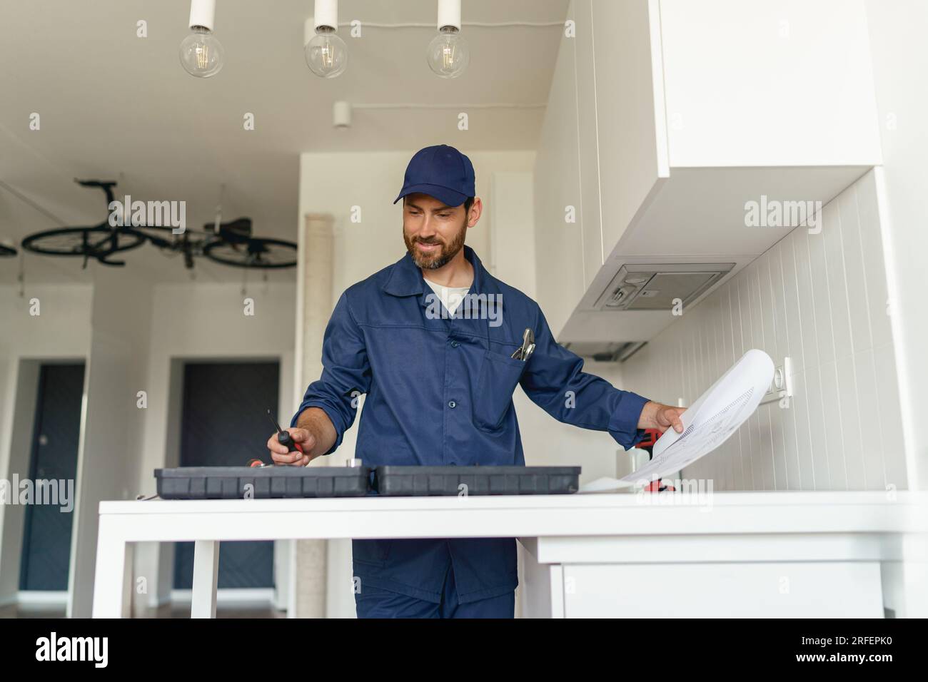 Handyman in uniform standing on kitchen with home plan and tool box ...