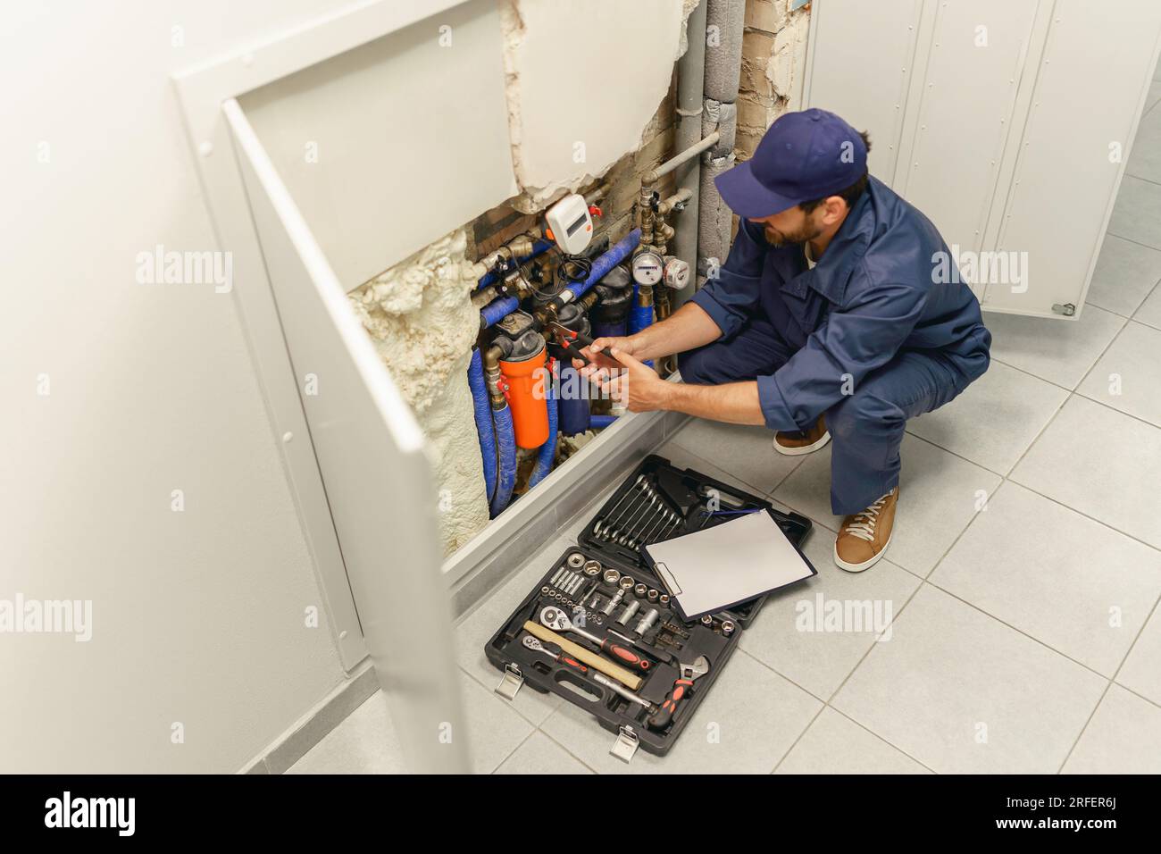 Handyman in uniform repairing water supply system at home uses an ...
