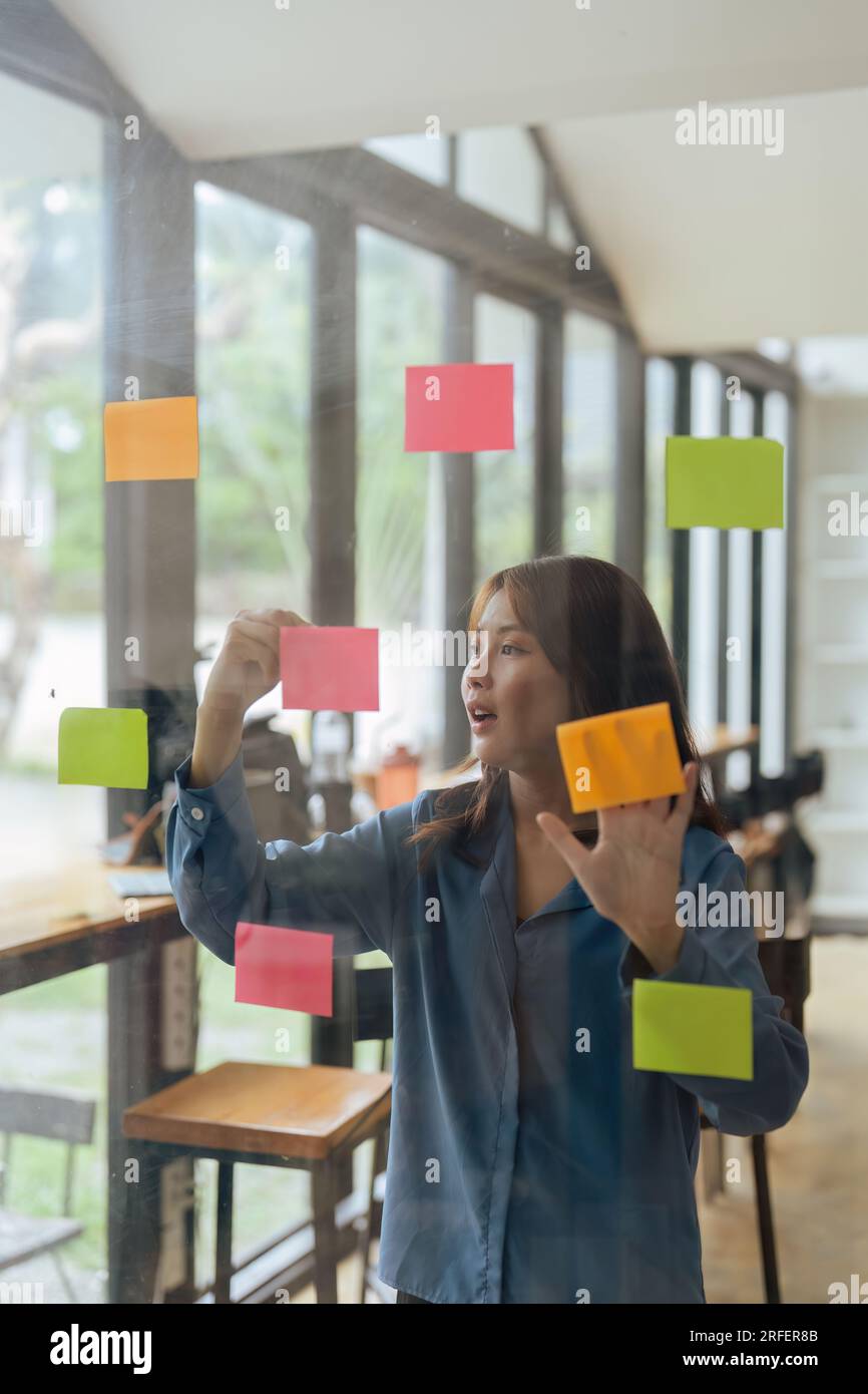 Thoughtful woman hand writing paper note, sticky note on glass window ...