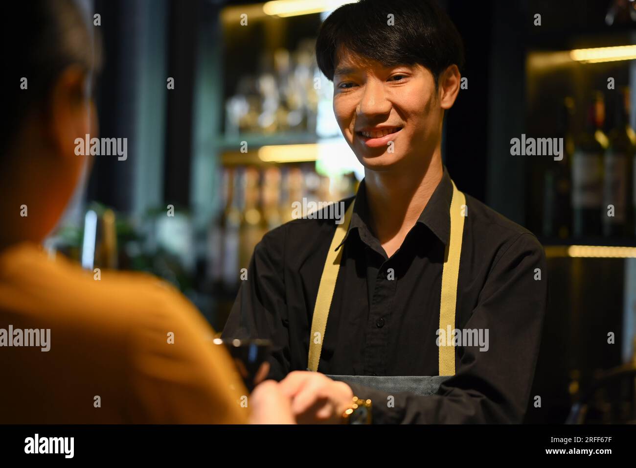 Friendly man barista wearing apron standing behind counter and serving ...