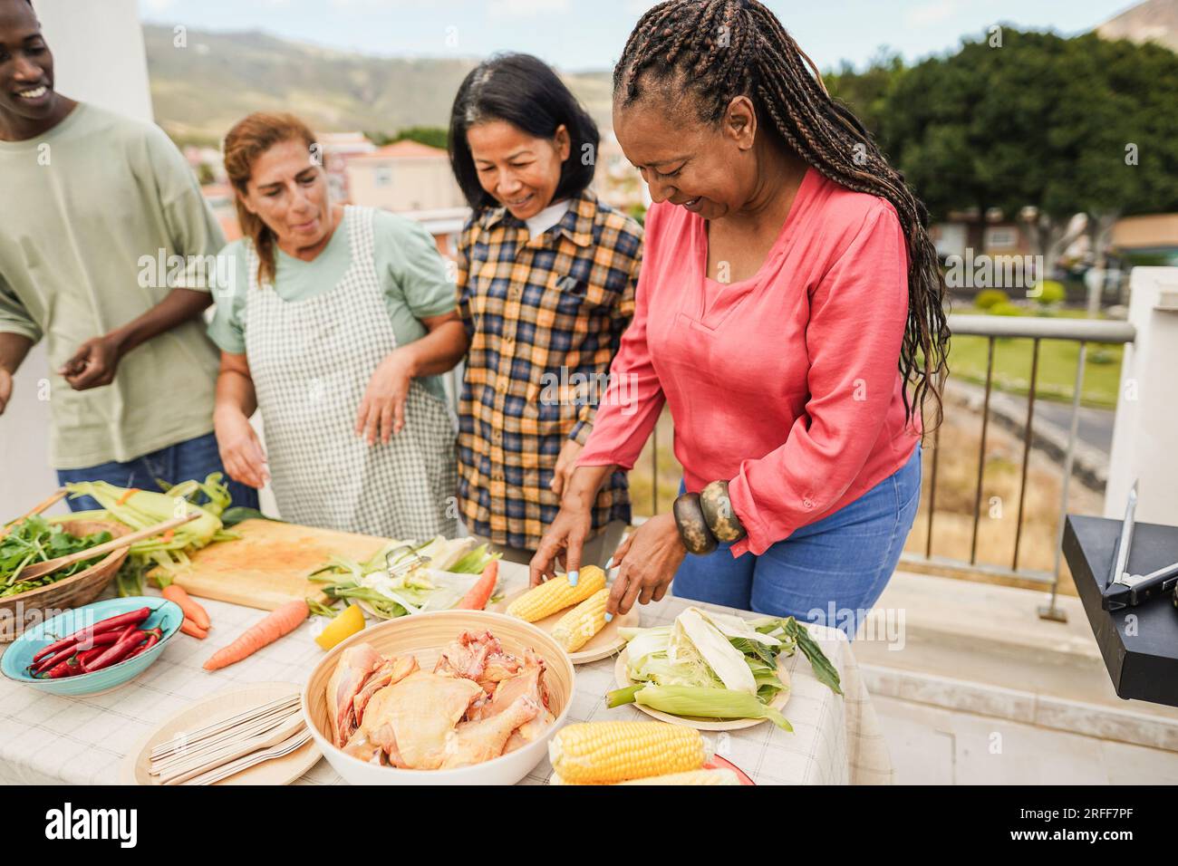 Happy multiracial women preparing food for barbecue at home's rooftop ...