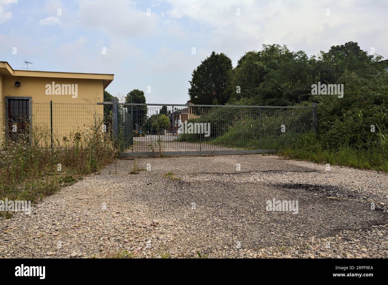 Gravel path blocked by a gate next to a building on a cloudy day in the ...