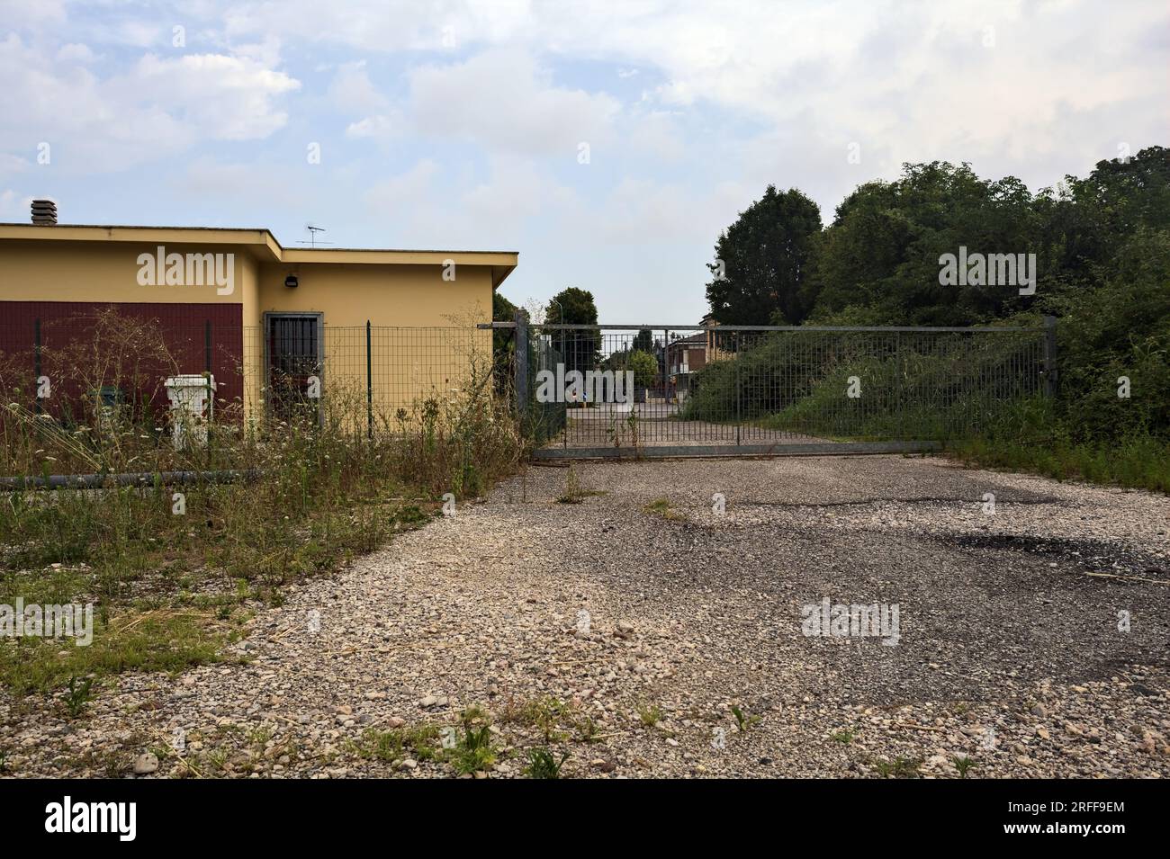 Gravel path blocked by a gate next to a building on a cloudy day in the ...