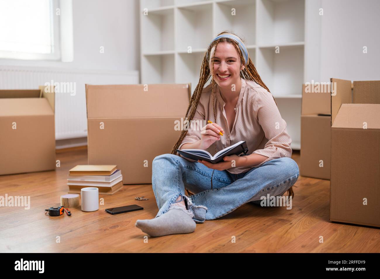 Modern ginger woman with braids writing in notebook while moving in new ...