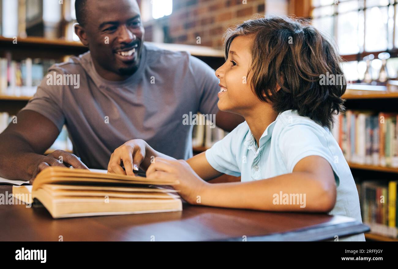 school teacher tutoring a young boy in a library. Male elementary ...