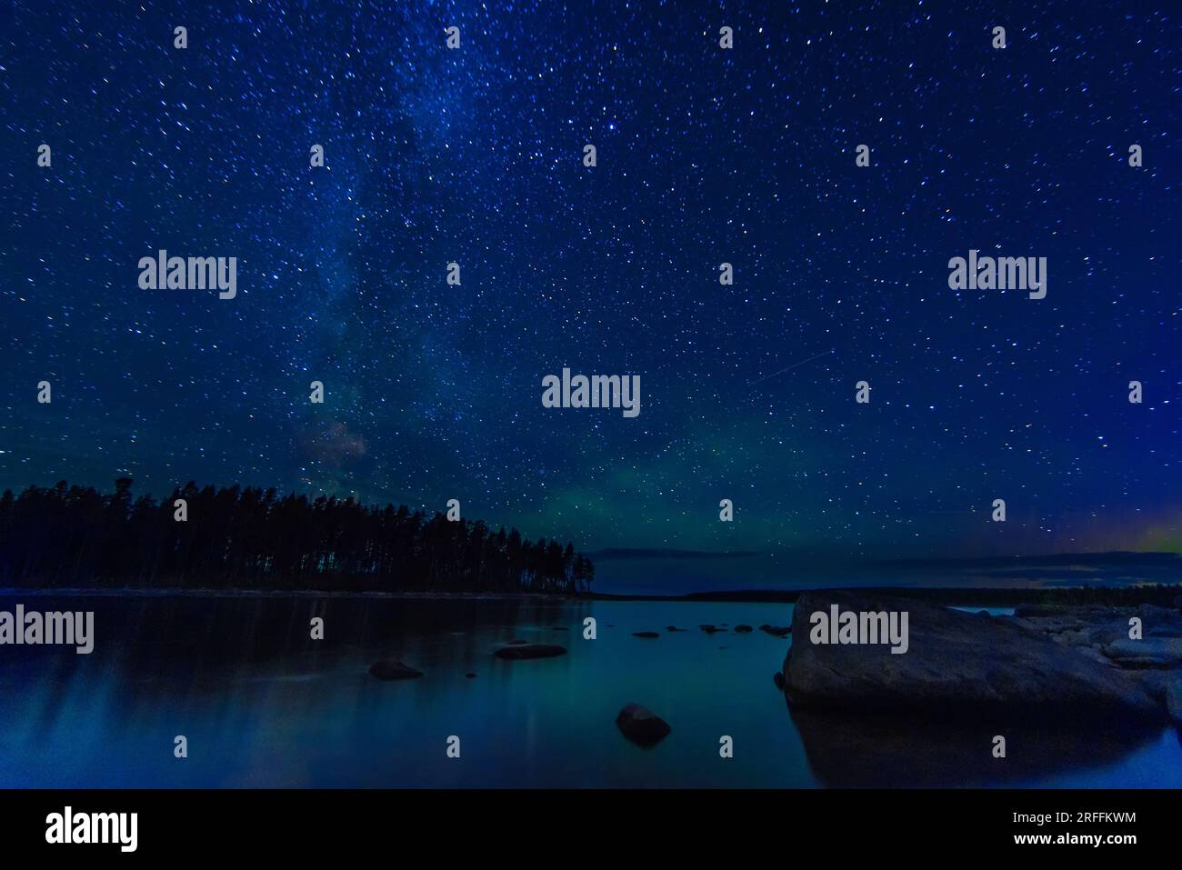 night landscape with a starry sky over sea water with stones and forest ...