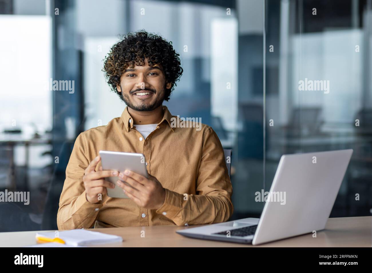 Portrait of young Indian programmer, man working inside company office, using laptop to write ...