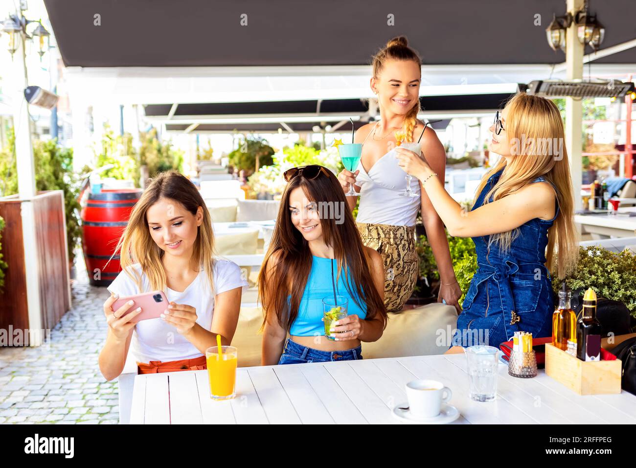 Trendy gen z girls watching viral video on mobile phone at cocktail bar ...