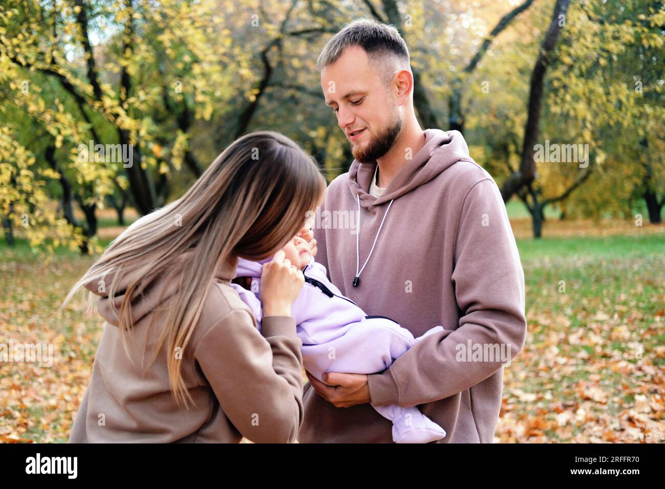 Parents on a walk with a baby in the autumn park. The baby is crying ...