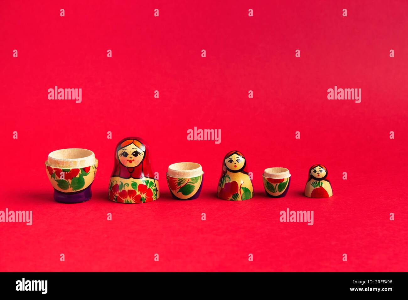 A set of wooden matryoshka dolls stand on a red background in order of ...