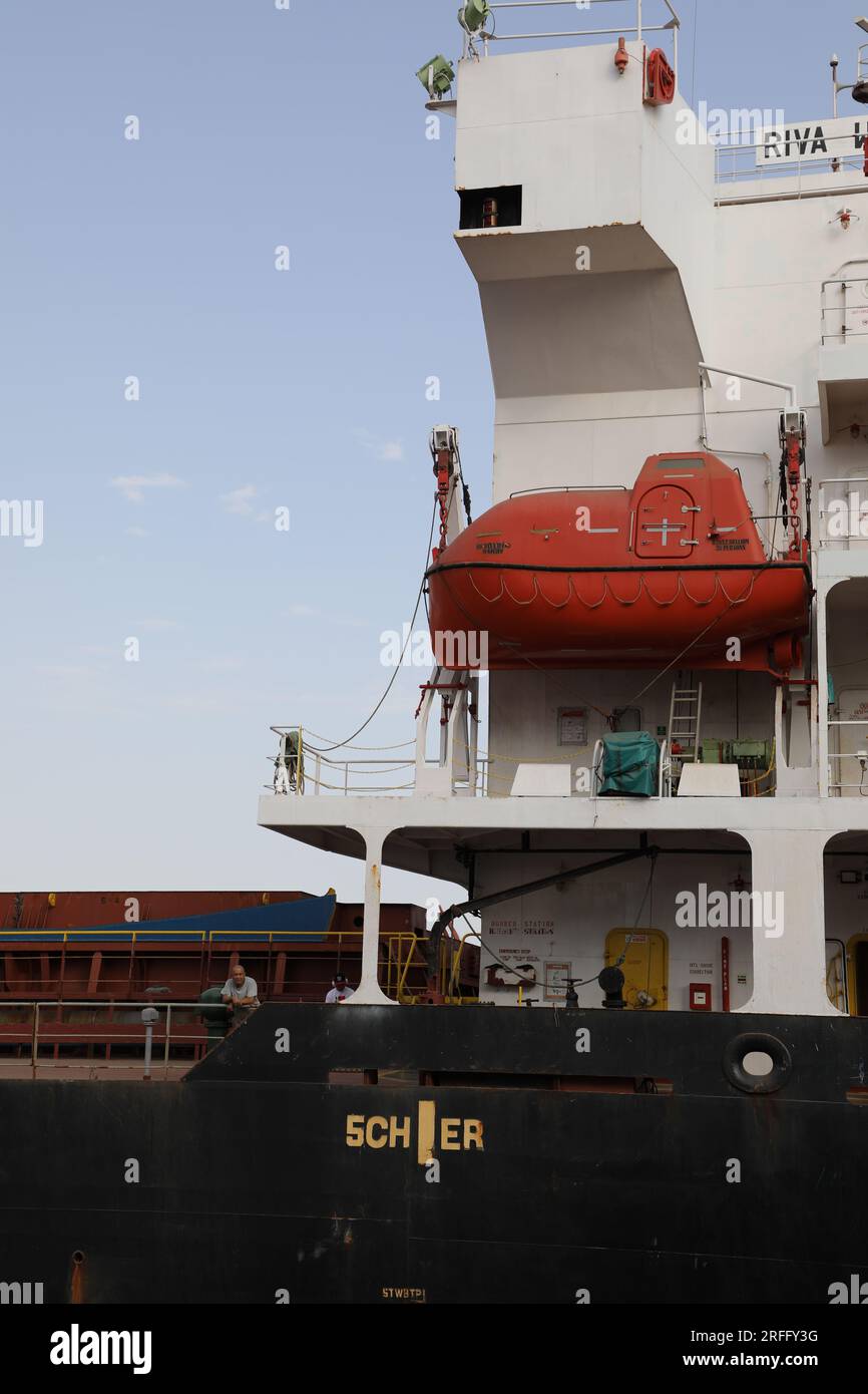 Closed, orange, rigid lifeboat hanging on board of a large ship (the ...