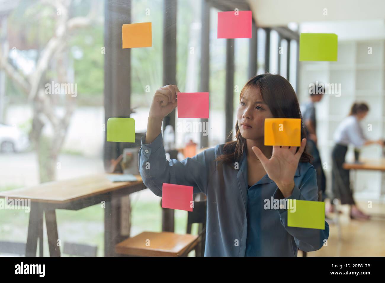 Thoughtful woman hand writing paper note, sticky note on glass window ...
