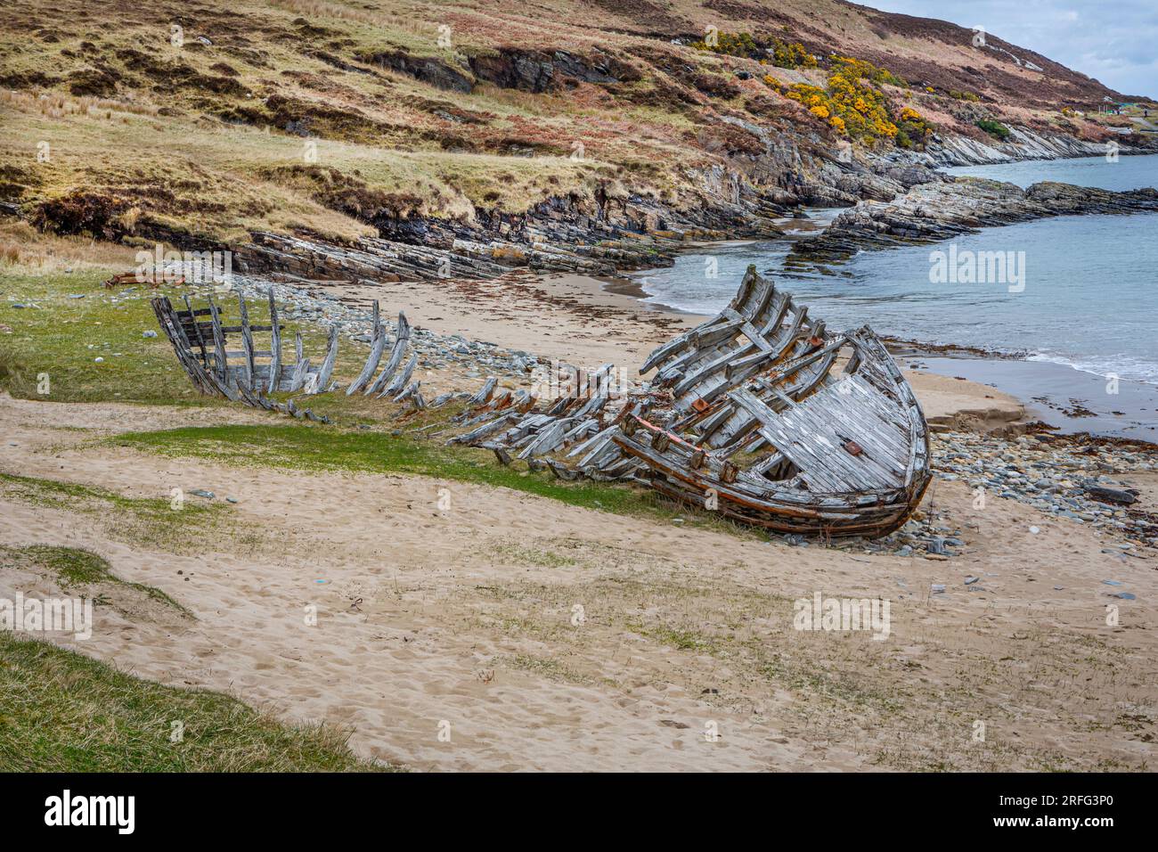 The skeleton of a ruined fishing boat on the beach in front of an old ...