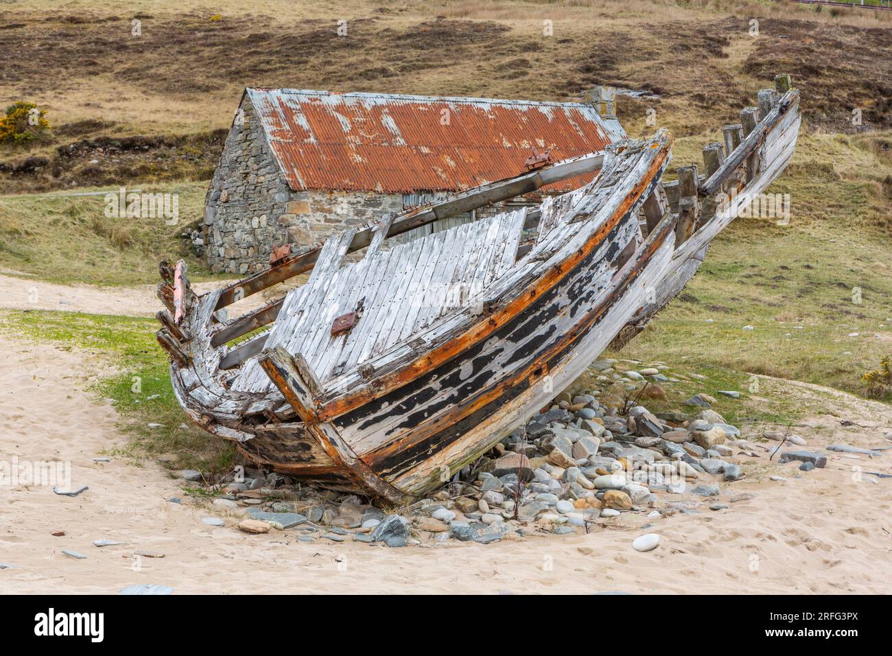 The skeleton of a ruined fishing boat on the beach in front of an old ...
