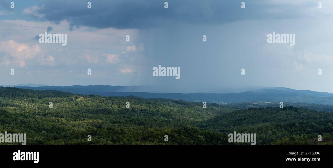 Cloudburst above hills overgrown in forests during summer, extreme ...