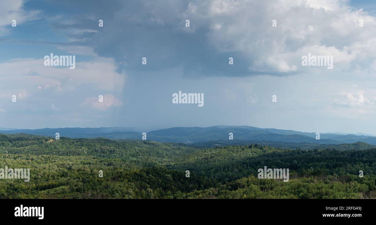 Cloudburst above hills overgrown in forests during summer, extreme ...