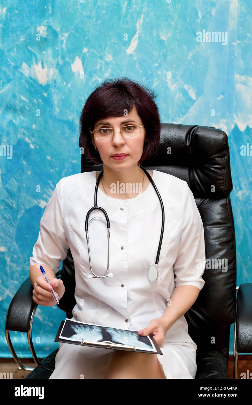 Woman doctor sits in a chair the office against a blue wall Stock Photo ...