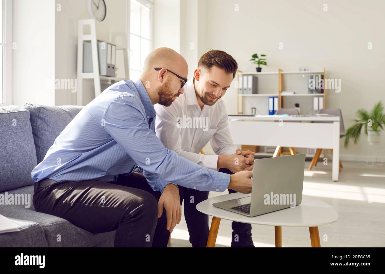Two young business men at work on laptop in office talking and having ...