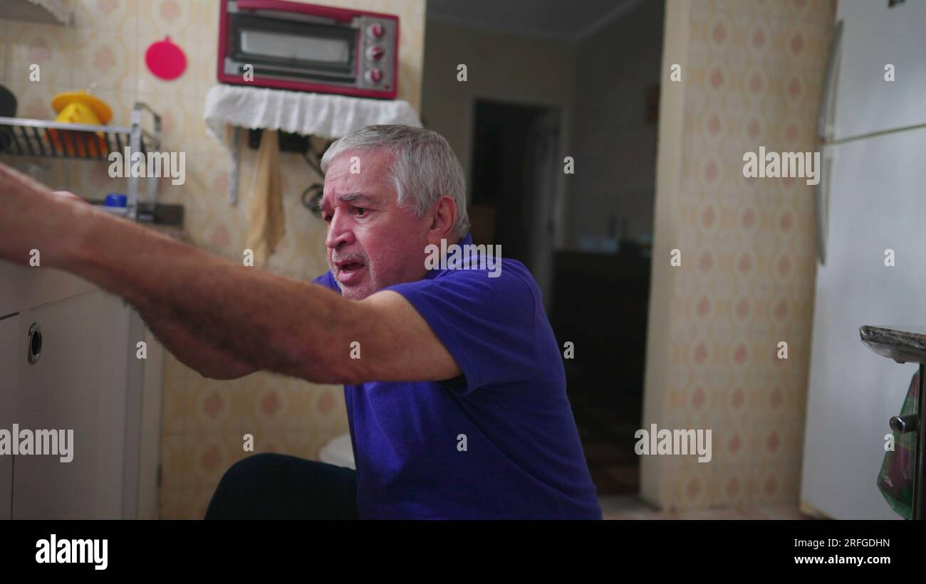 Senior man suffering heart attack alone at home leaning on kitchen sink ...